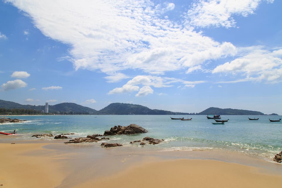 Uma praia com águas azul-claras, barcos e montanhas ao fundo.