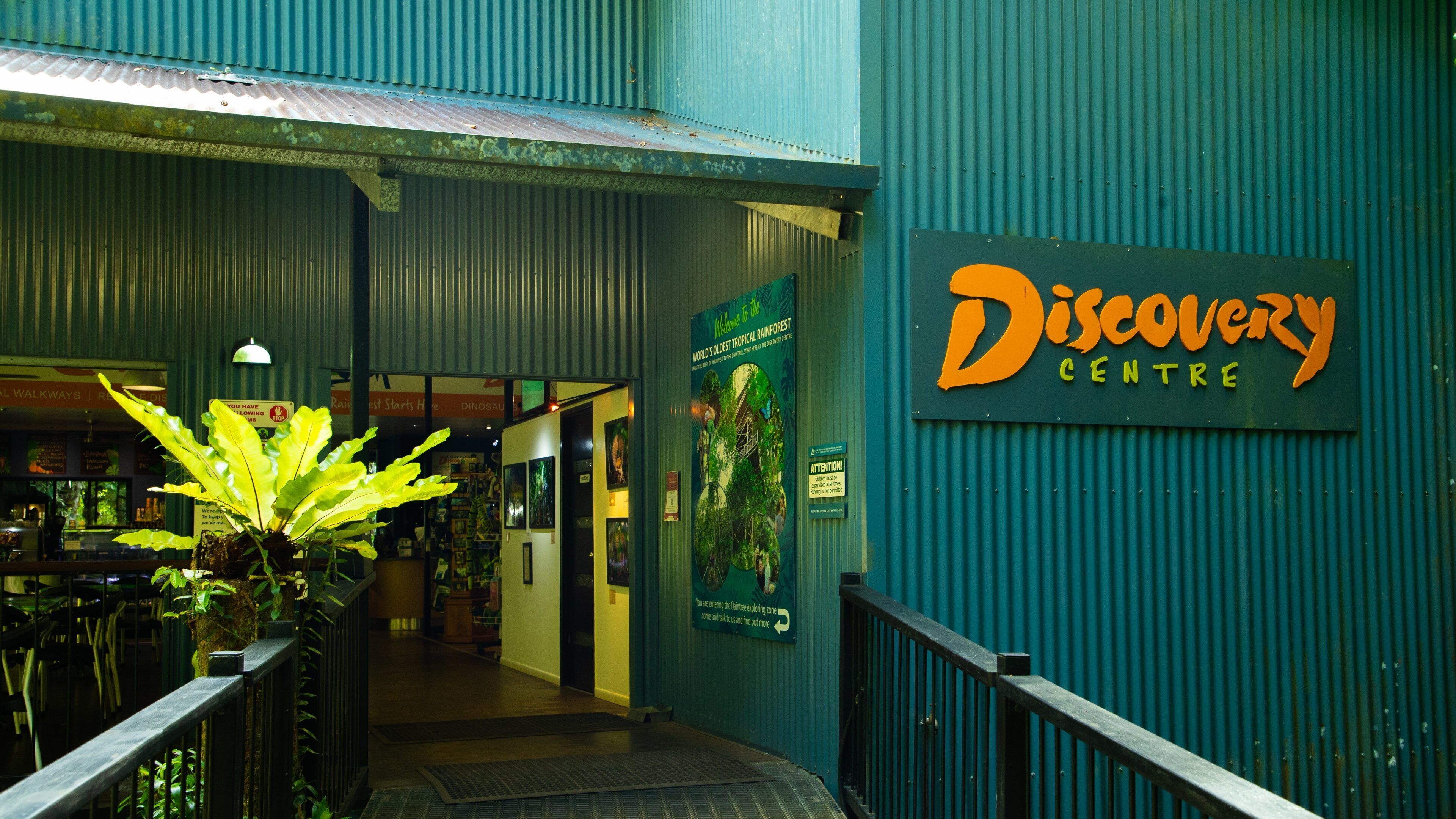 A entrada do Discovery Centre, com uma placa, uma escadaria e um vaso de planta grande.