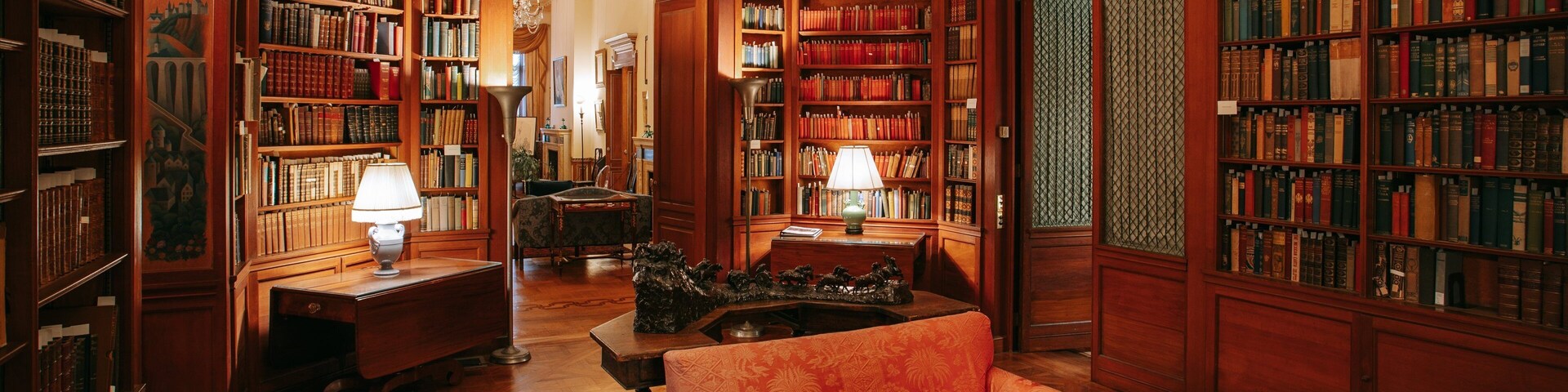Uma biblioteca com estantes de madeira, uma poltrona vermelha e um quadro na parede.