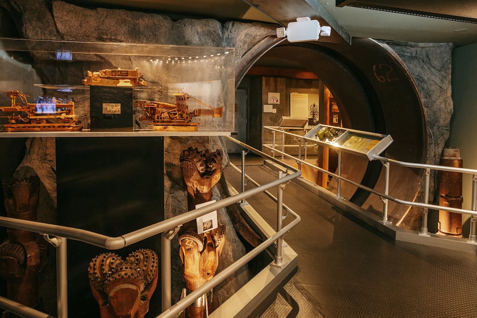 Exposição de museu com equipamentos de mineração e uma escadaria.