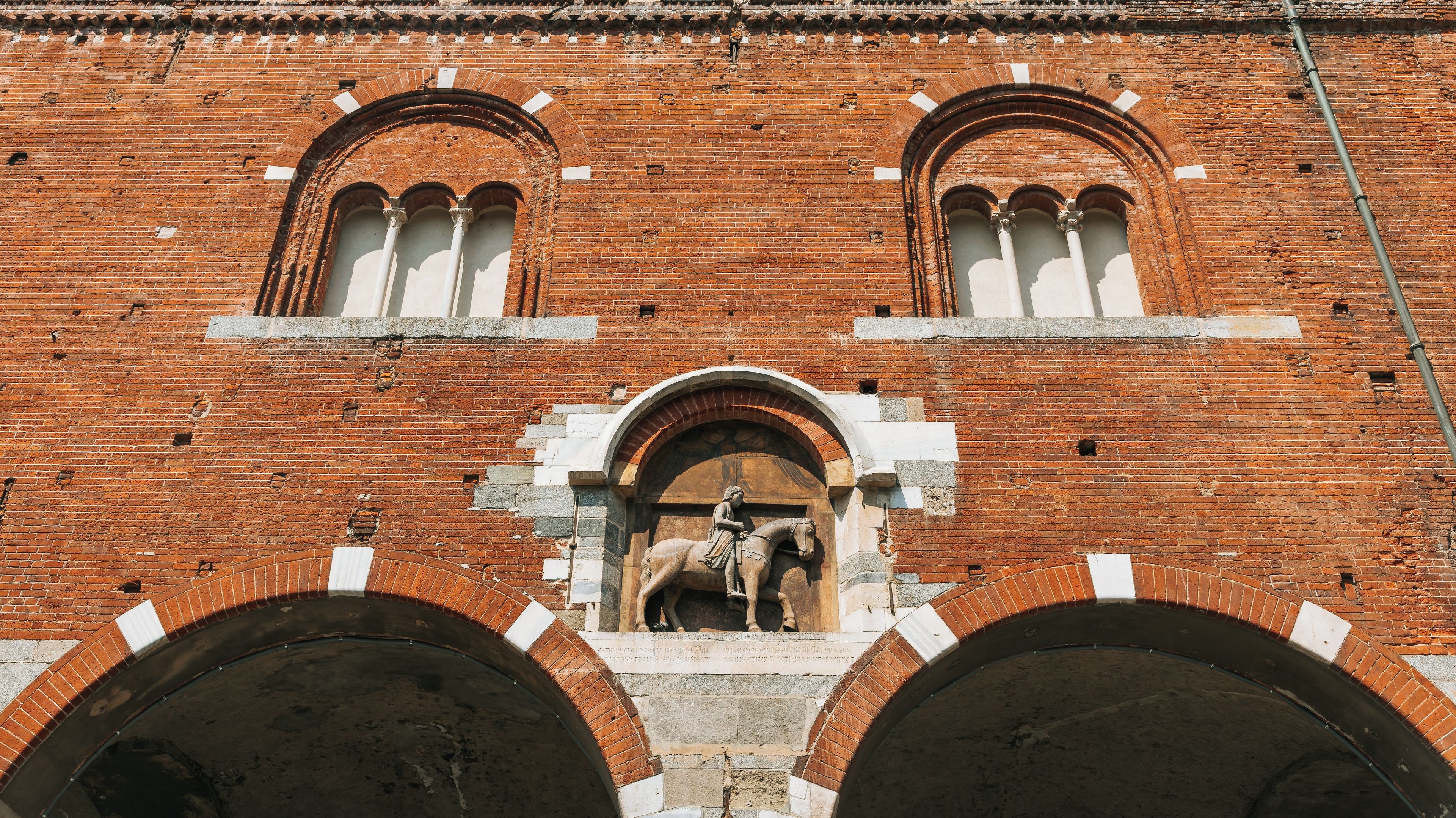 Um edifício de tijolos vermelhos com janelas em arco e uma estátua de uma figura montada a cavalo.