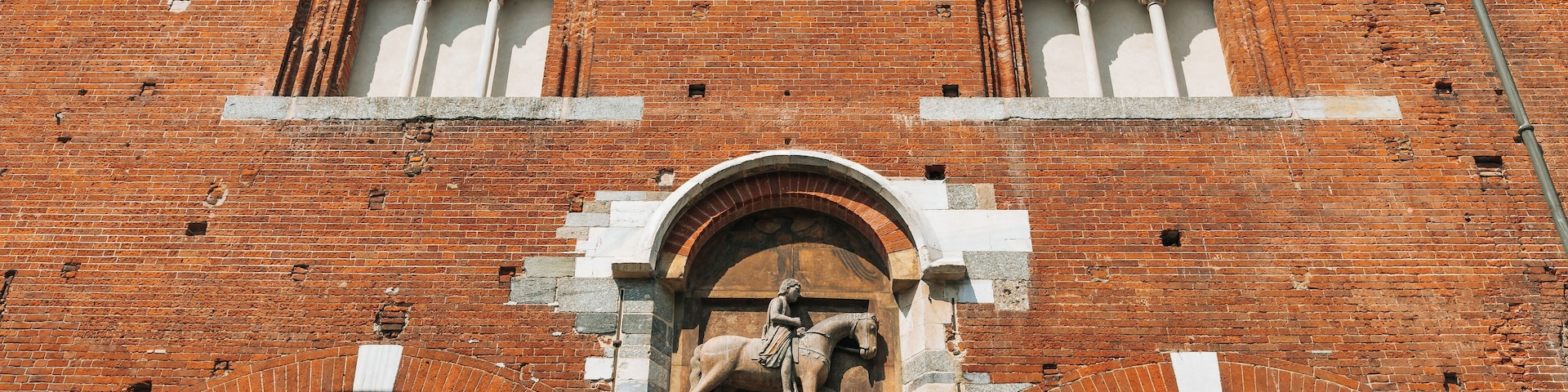 Um edifício de tijolos vermelhos com janelas em arco e uma estátua de uma figura montada a cavalo.