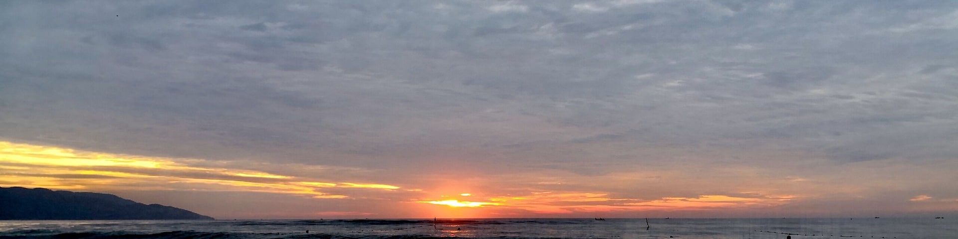Praia ao pôr do sol com ondas e céu nublado.