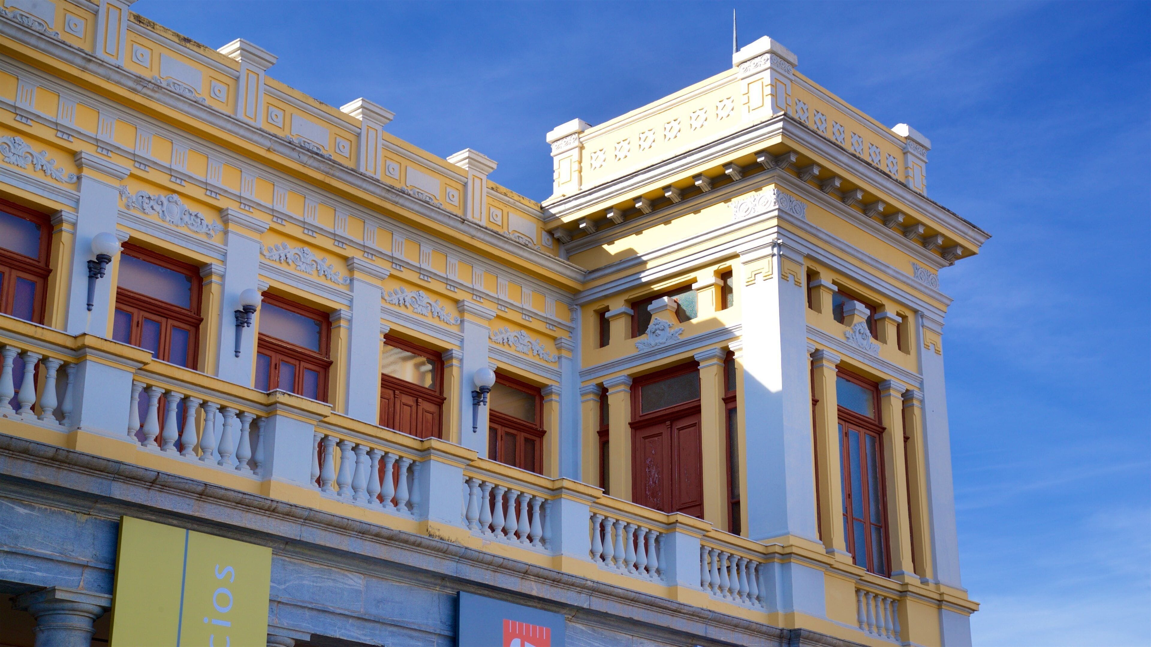 Um edifício amarelo com varandas elaboradas e molduras de janelas vermelhas.