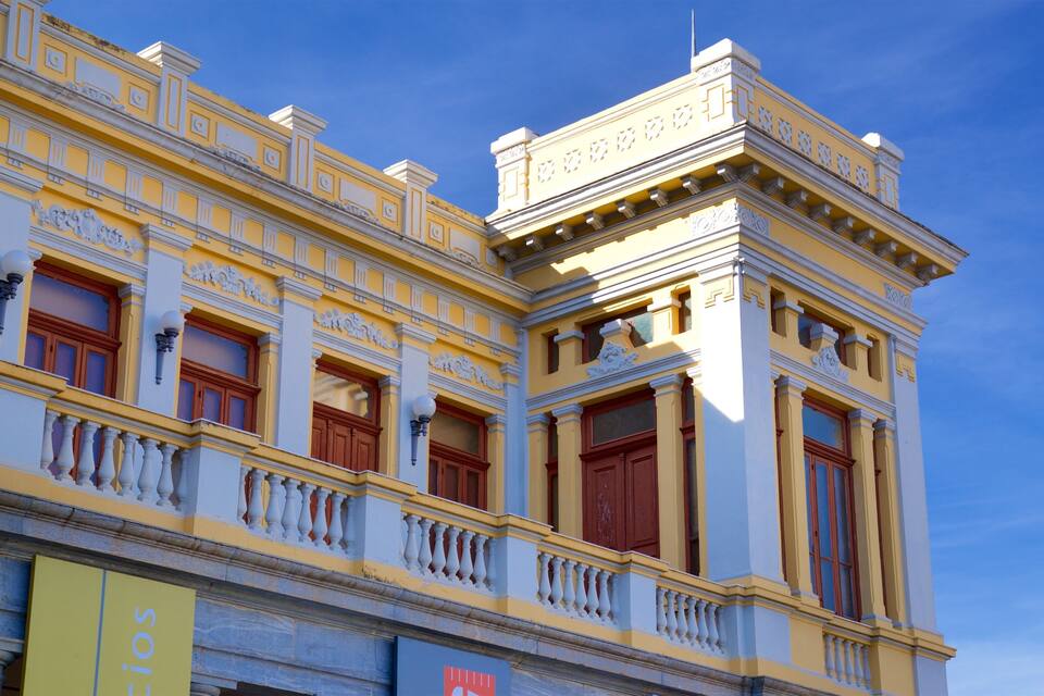 Um edifício amarelo com varandas elaboradas e molduras de janelas vermelhas.