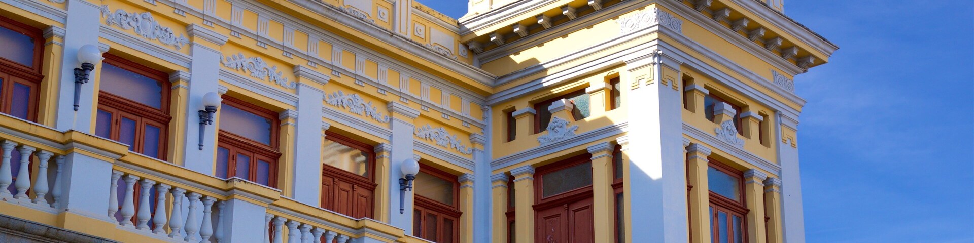 Um edifício amarelo com varandas elaboradas e molduras de janelas vermelhas.