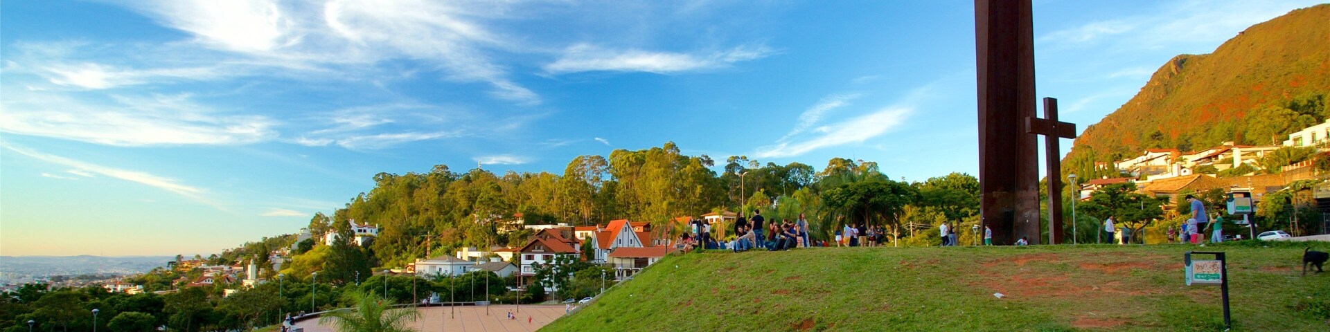 Um parque com um monumento imponente, uma área pavimentada e uma encosta com casas ao fundo.