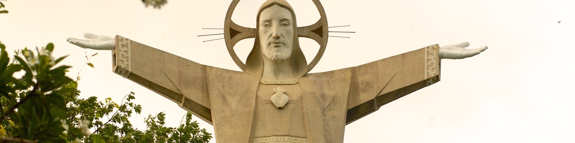Uma grande estátua com braços estendidos e um halo circular, rodeada por vegetação.