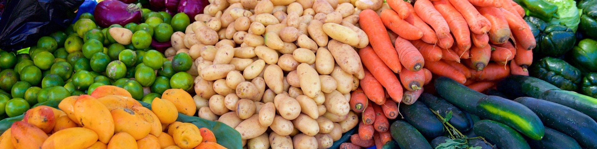 Diversos vegetais frescos, como batatas, cenouras e pepinos, expostos em uma feira.