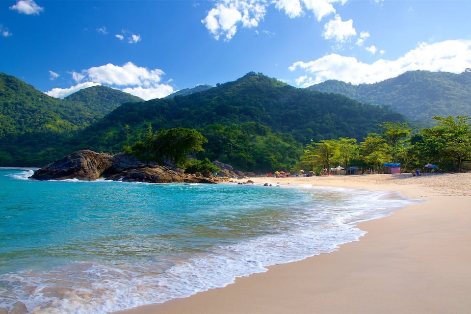 Uma praia com águas azul-turquesa, areal arenoso e montanhas verdes ao fundo.