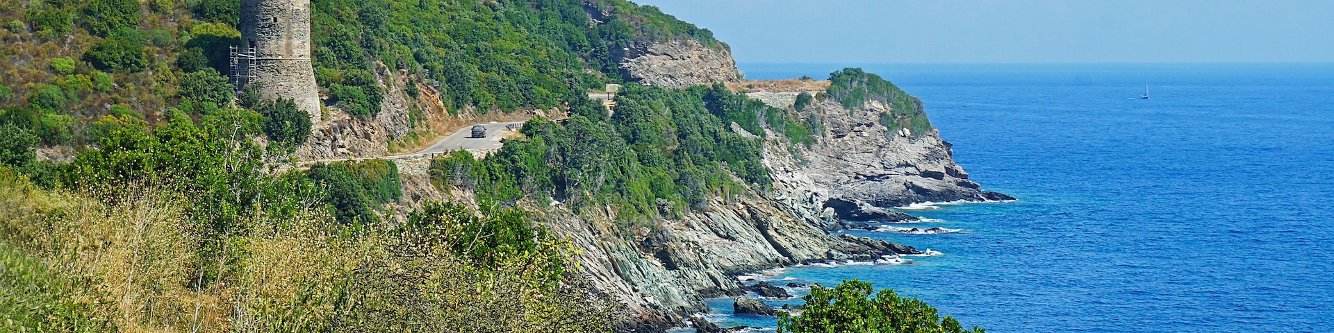 Paisagem costeira com uma torre de pedra numa encosta, com vista para o mar.