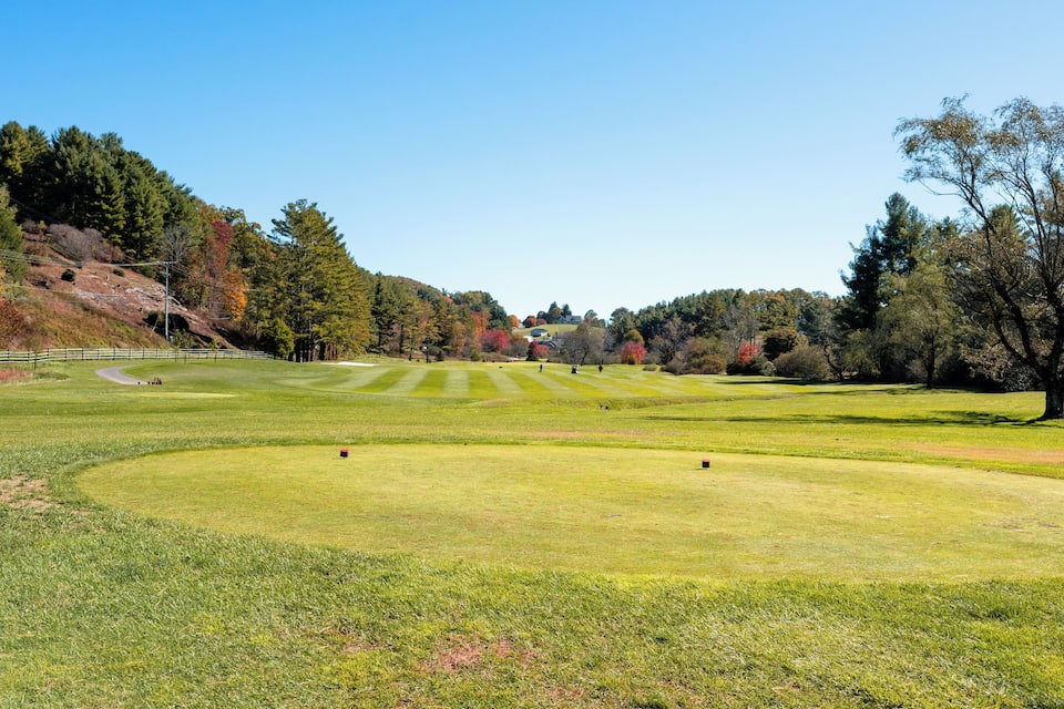 Um campo de golfe com céu limpo, grama verde e árvores ao fundo.