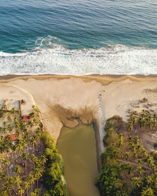 Vista aérea de uma área costeira com praia, um corpo de água pequeno e palmeiras.