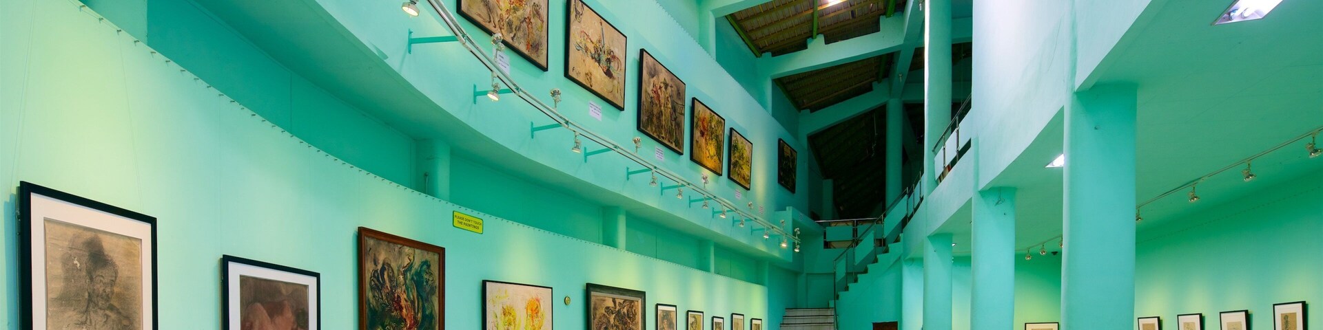 Uma galeria com obras de arte em paredes verde-água e piso de madeira.