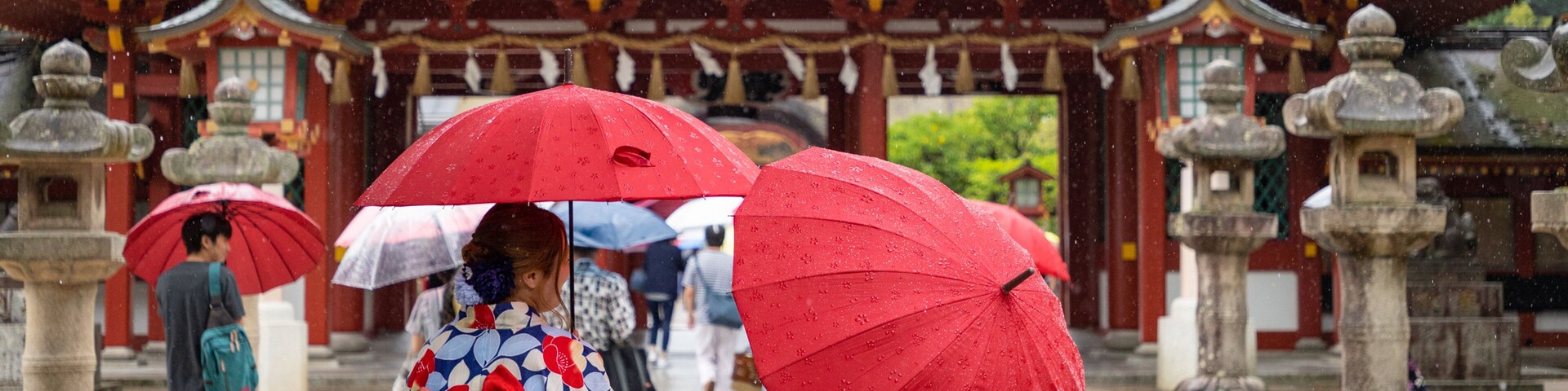 Um templo japonês tradicional com guarda-chuvas vermelhos segurados por visitantes.