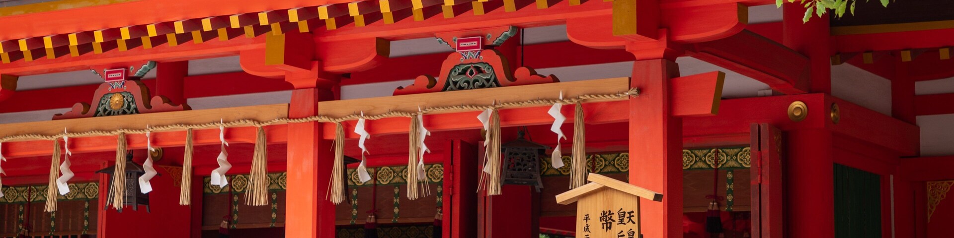 Um edifício japonês tradicional com pilares vermelhos e uma placa de madeira com caracteres japoneses.