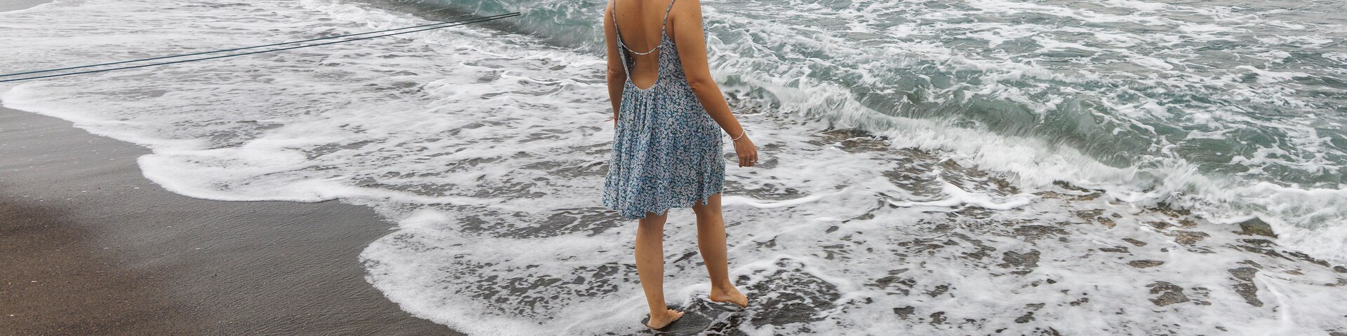 Uma mulher em pé na praia, com ondas se aproximando.
