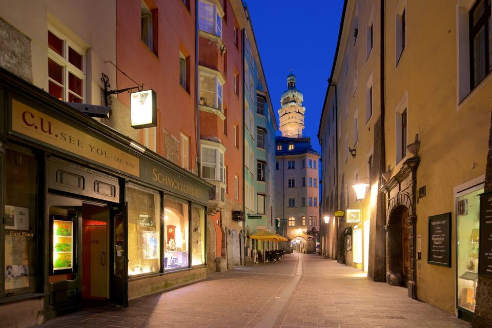 Rua estreita com edifícios coloridos, uma torre com cúpula e letreiros iluminados.