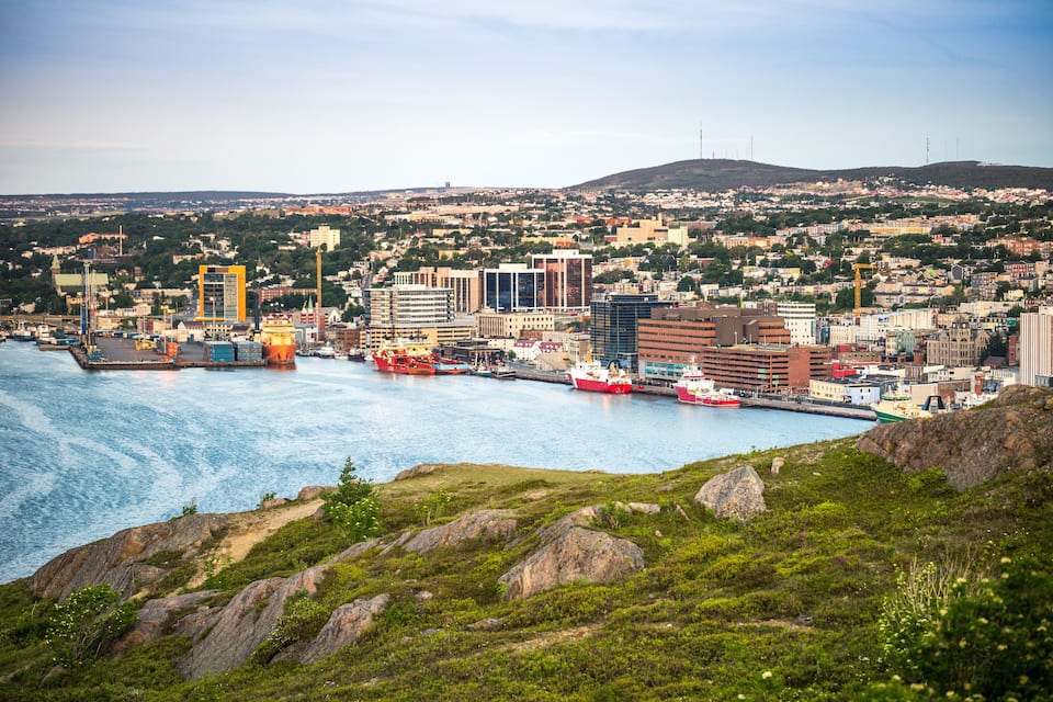 Paisagem costeira urbana com um porto, incluindo barcos, edifícios e um horizonte montanhoso.