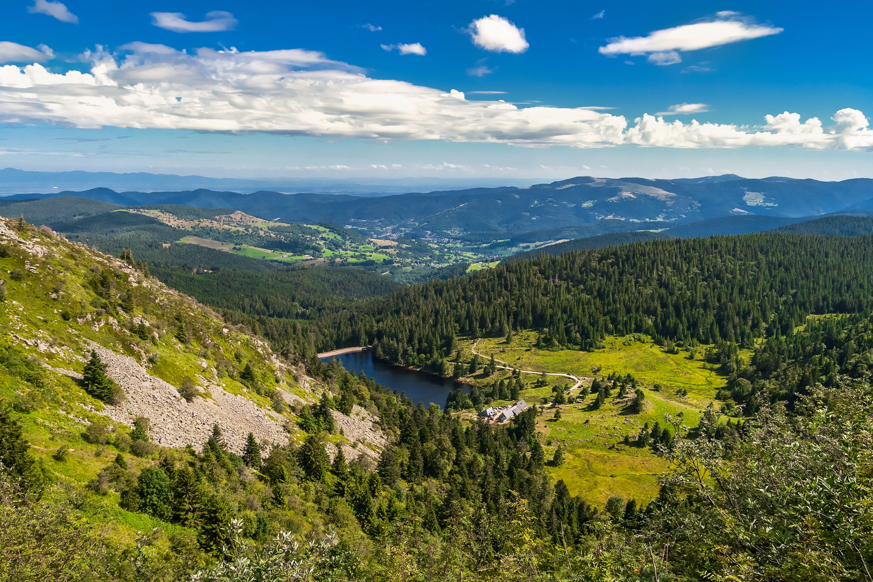Paisagem montanhosa com um lago, florestas densas e colinas ondulantes.