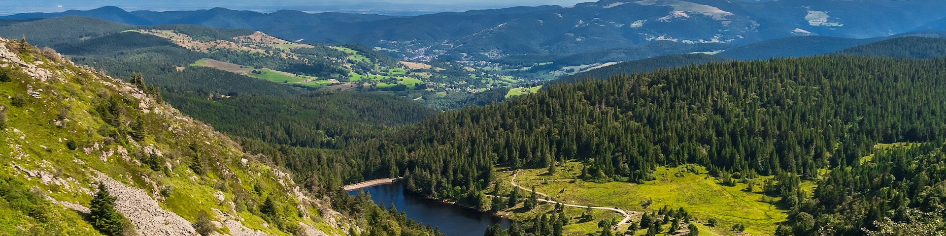 Paisagem montanhosa com um lago, florestas densas e colinas ondulantes.