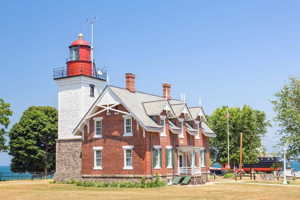 Um edifício histórico de tijolos com um farol vermelho, um alpendre branco e um barco atracado nas proximidades.
