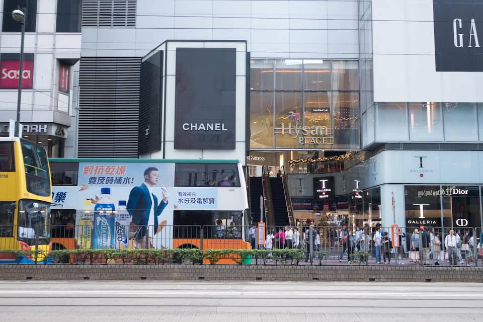 Uma área urbana movimentada para compras, com lojas de destaque como Chanel e Hysan Plaza.
