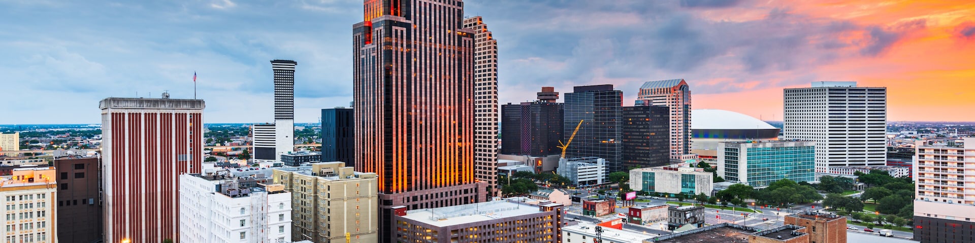 Horizonte urbano com um edifício alto imponente, vários edifícios de altura média e um céu ao pôr do sol.