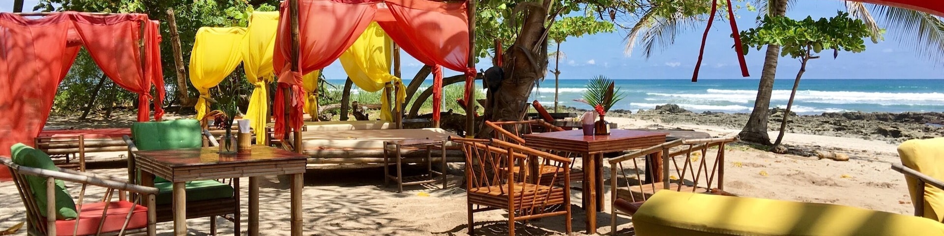 Um café à beira-mar com mobiliário de bambu e toldos vermelhos e amarelos.
