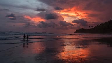 Uma praia com pessoas caminhando, ondas e um céu ao pôr do sol.