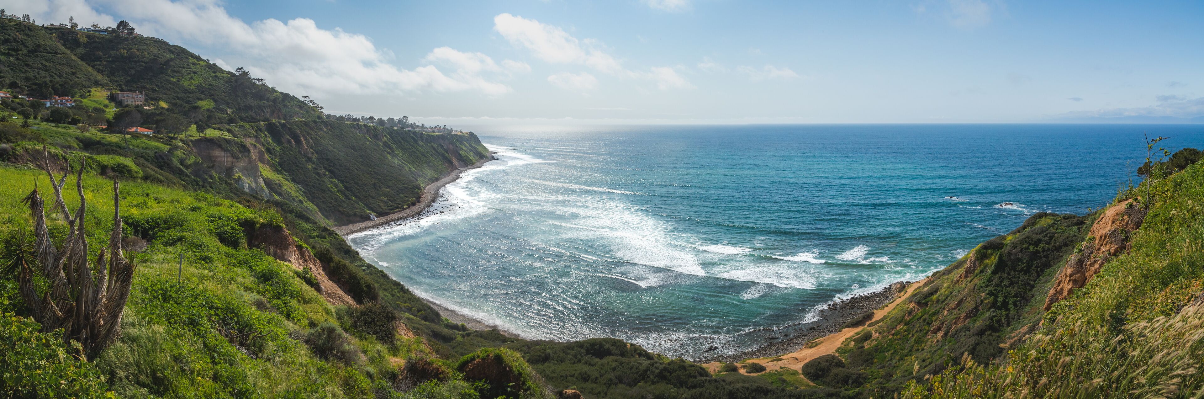 Paisagem costeira com penhasco, oceano e uma aldeia distante.