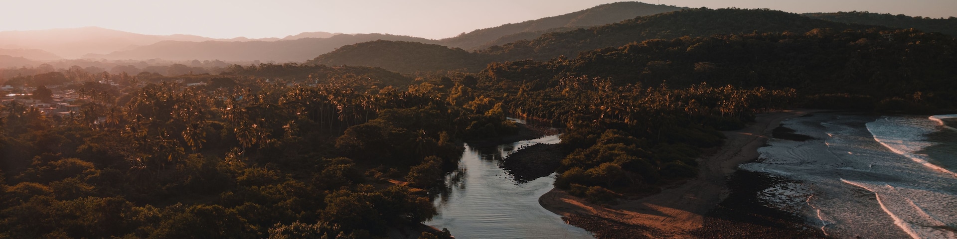Um rio serpenteando por um vale densamente florestado, com colinas ao fundo.
