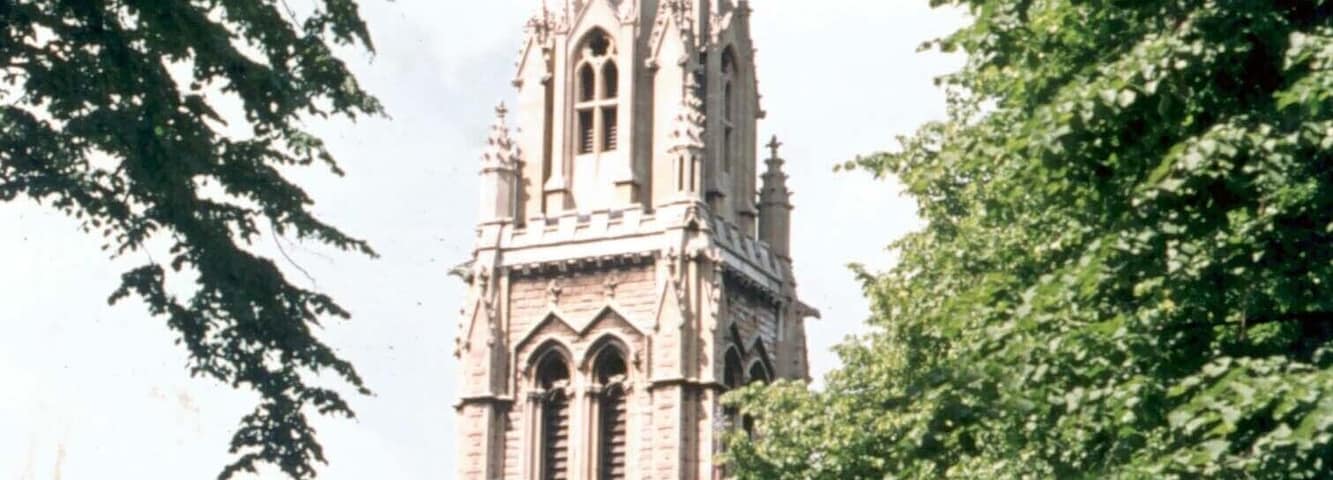 Uma igreja alta com um pináculo pontiagudo, rodeada por árvores.