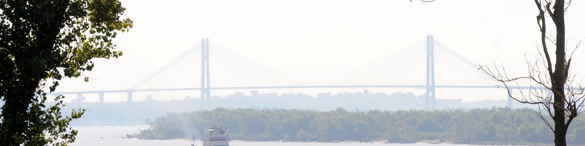 Um grupo de pessoas voando pipas perto de um rio, com uma ponte ao fundo.