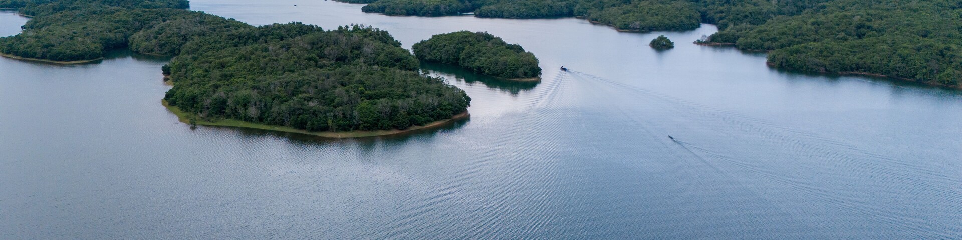 Vista aérea de um grande lago rodeado por floresta densa e montanhas ao longe.