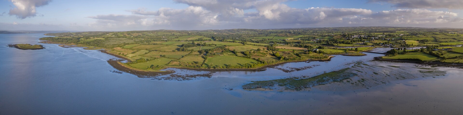 Paisagem costeira com campos verdes, uma pequena cidade e uma vasta extensão de água.