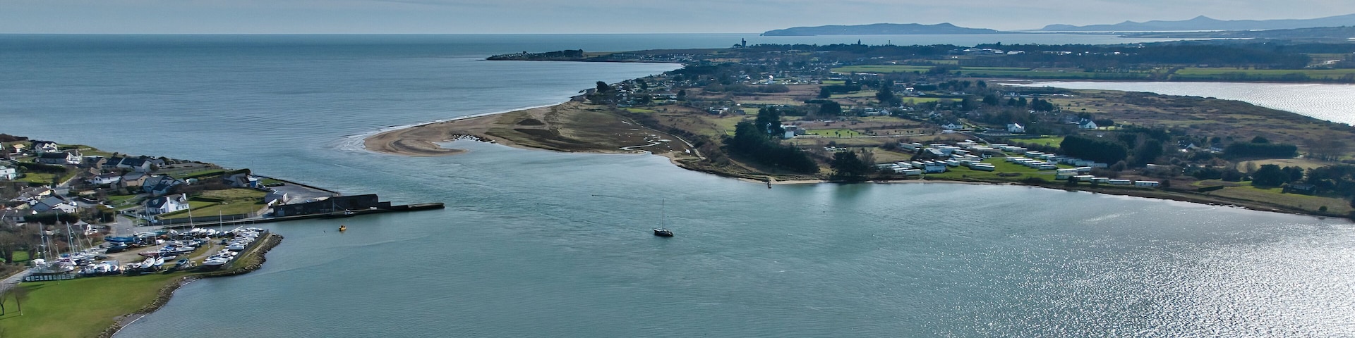 Uma vila costeira com um porto, praia de areia e uma pequena ilha.