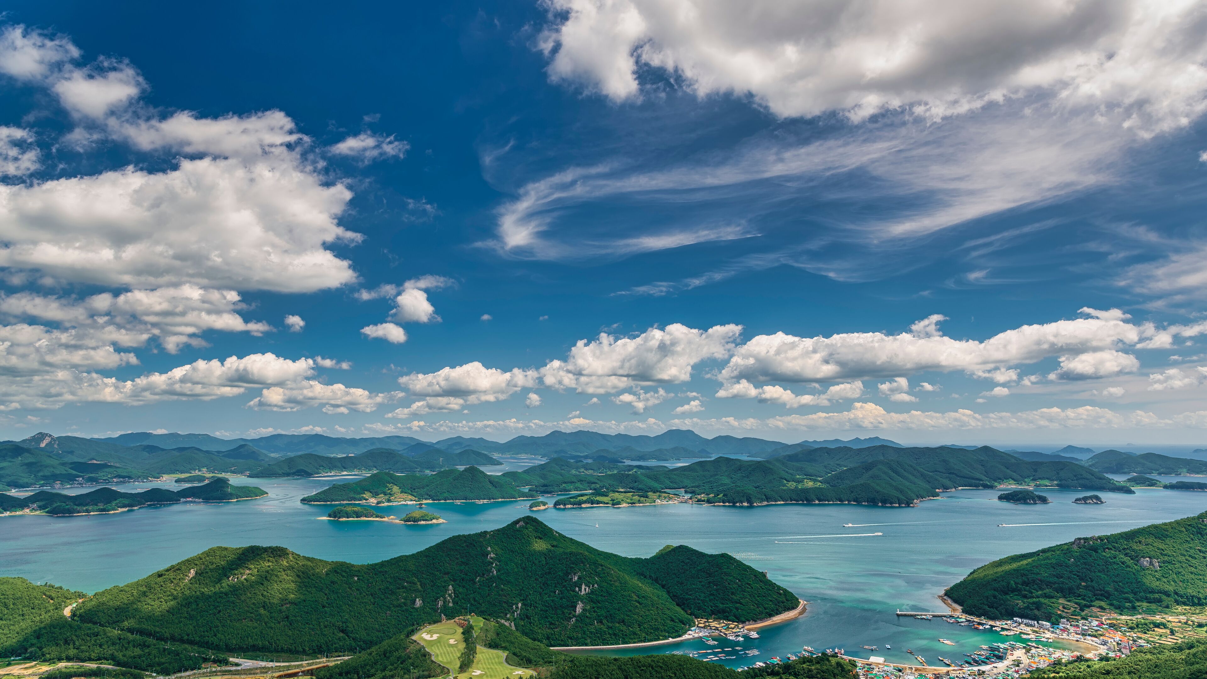 Paisagem costeira com colinas verdejantes, uma baía de águas cristalinas e uma pequena cidade com edifícios próximos à praia.