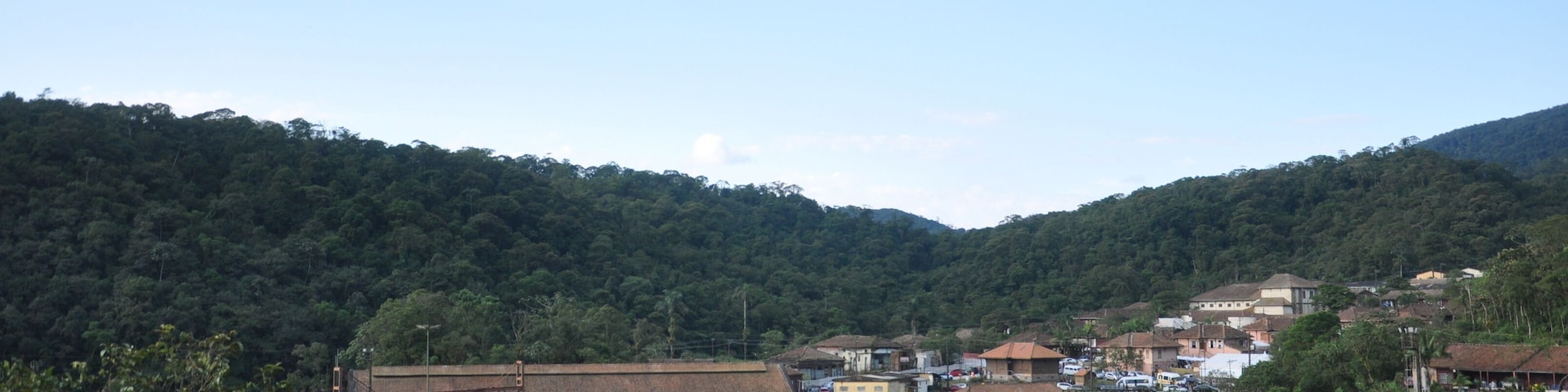 Uma ponte com pessoas atravessando sobre um trilho de comboio, rodeada por uma paisagem acidentada e edifícios.