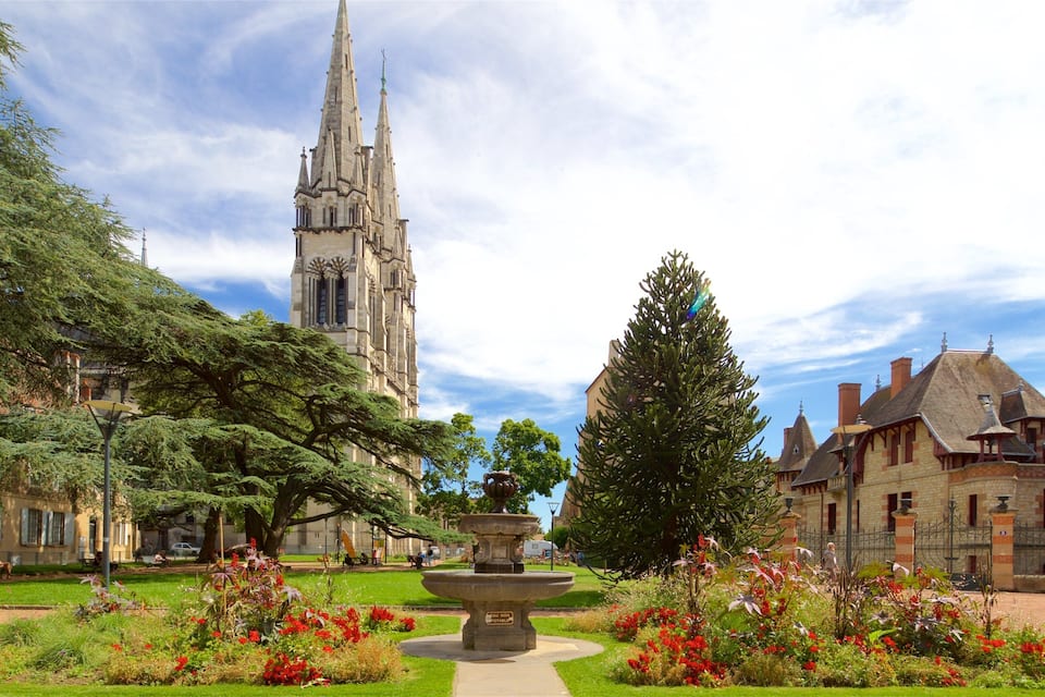 Uma igreja histórica com uma torre alta, uma fonte central e jardins exuberantes ao redor.