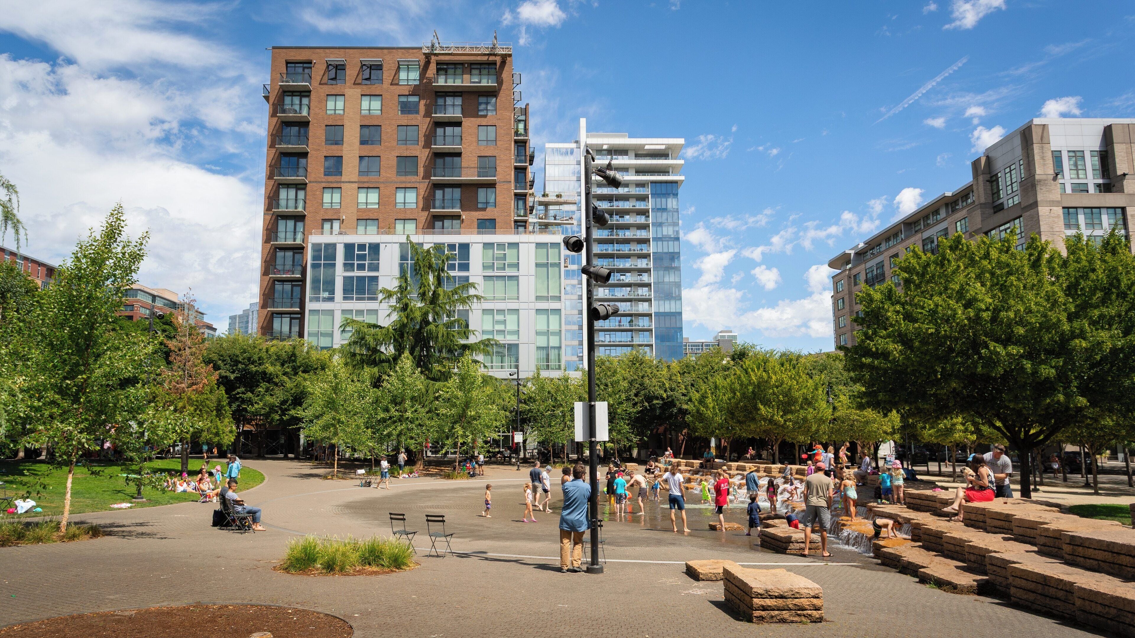 Lively summer afternoon at Jamison Square in the Pearl District of Portland, Oregon with families enjoying the outdoors and modern architecture in the background