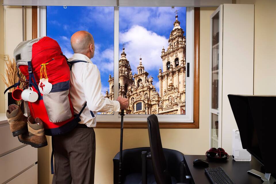 Um homem com uma mochila observando uma janela com vista para uma catedral.
