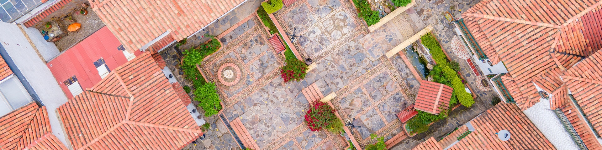 Vista aérea de um pátio com telhados de telha vermelha, caminhos de pedra e plantas verdes.