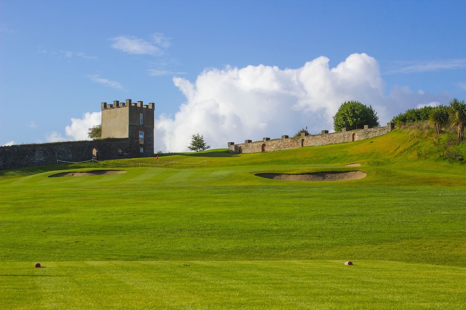 Um campo de golfe com bunkers, um castelo e um céu azul e límpido.
