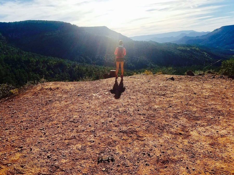 Uma pessoa caminhando por uma trilha de terra com paisagem montanhosa ao fundo.