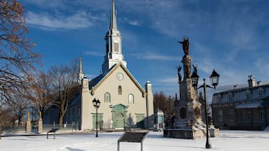 Igreja com uma torre alta e uma estátua numa praça coberta de neve.
