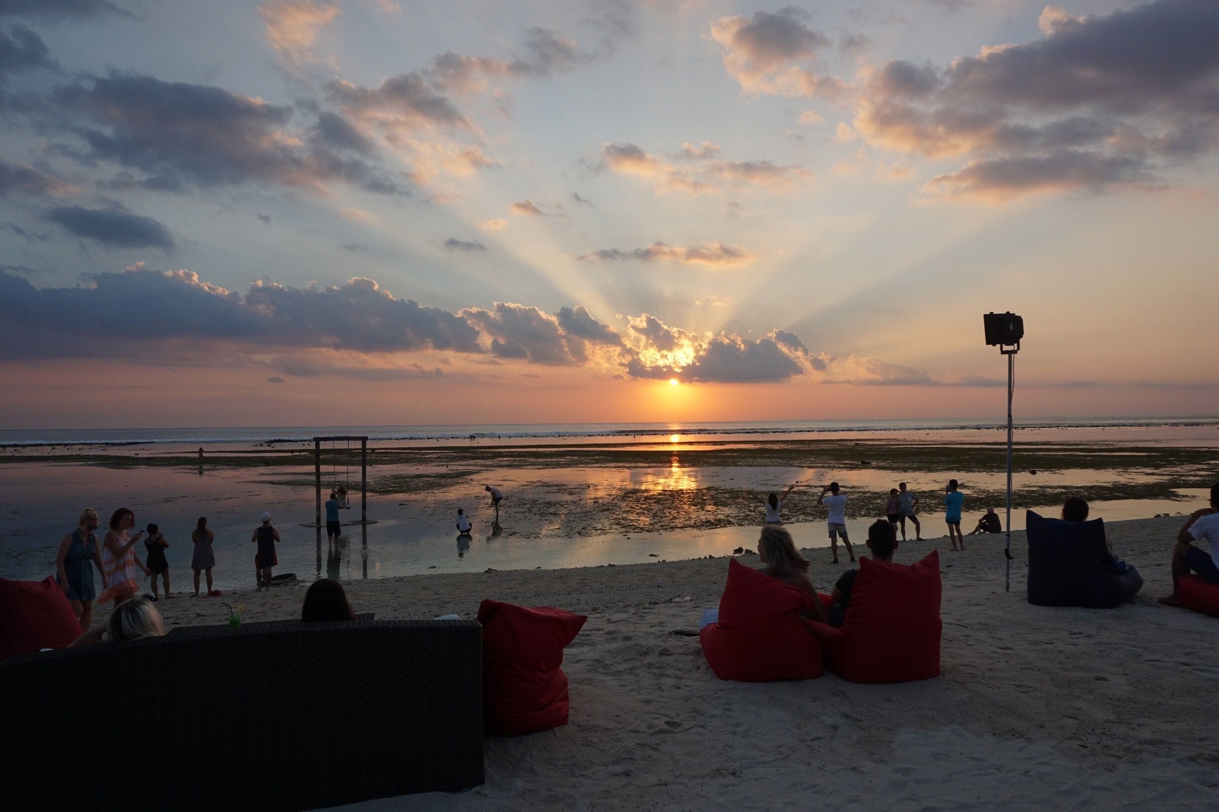 Praia ao pôr do sol com pessoas e cadeiras de praia.