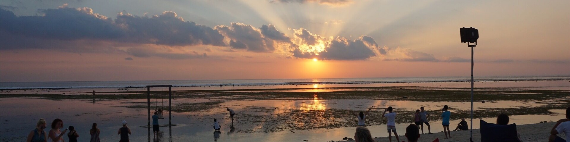 Praia ao pôr do sol com pessoas e cadeiras de praia.