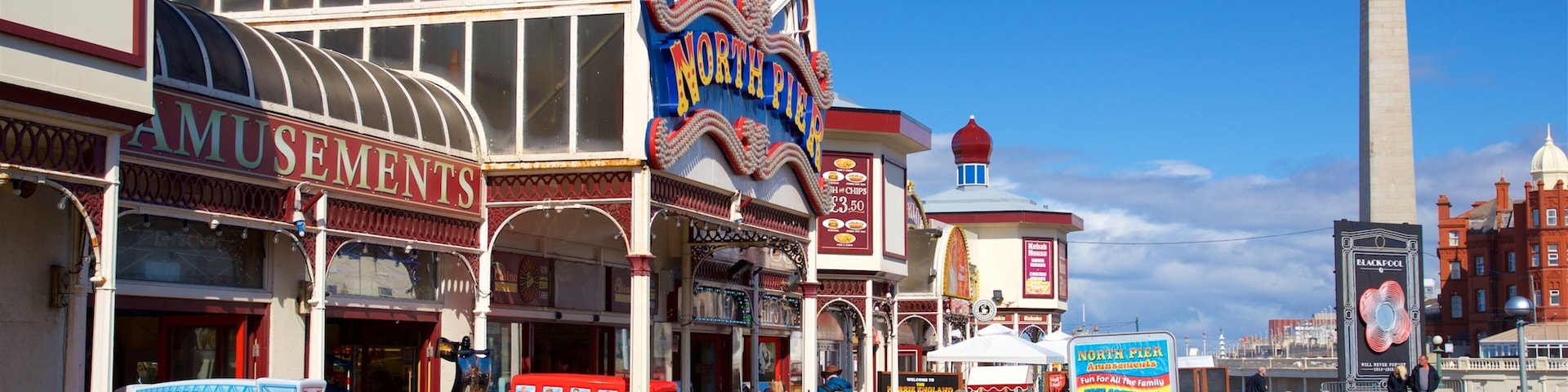 Rua com roda gigante, placa indicando North Pier Amusements e um monumento grande ao fundo.