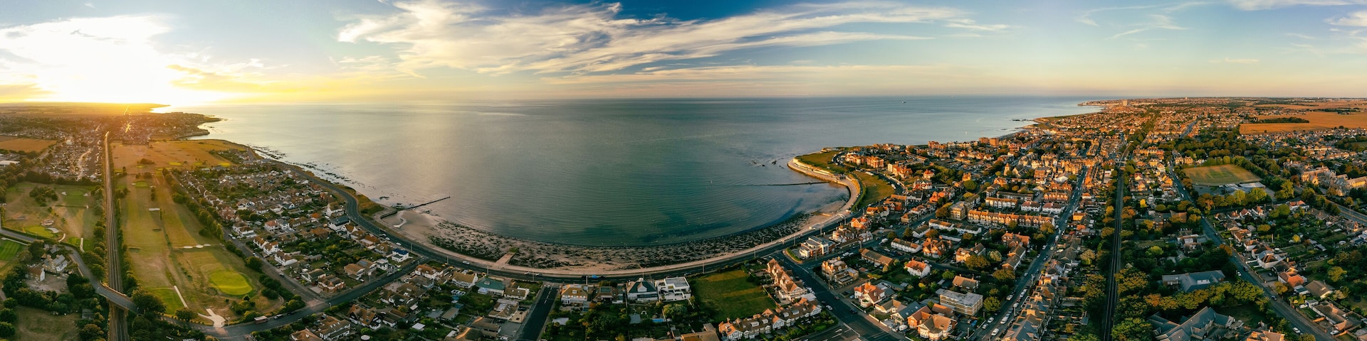 Vista aérea de uma cidade costeira com uma estrada sinuosa, áreas residenciais e uma grande massa de água.
